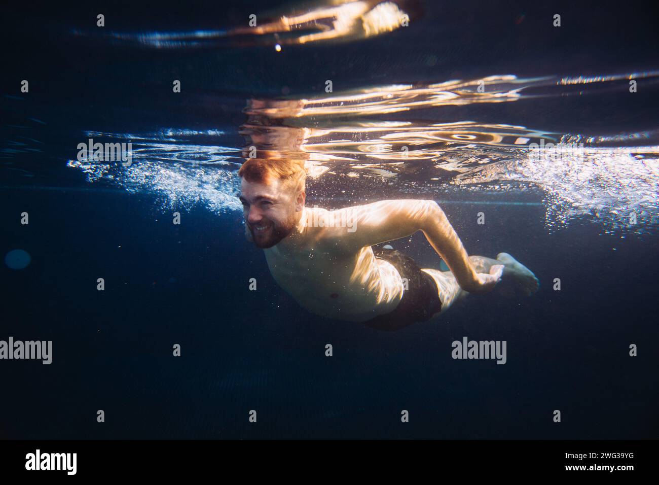 A handsome young man swims underwater in a swimming pool while on ...
