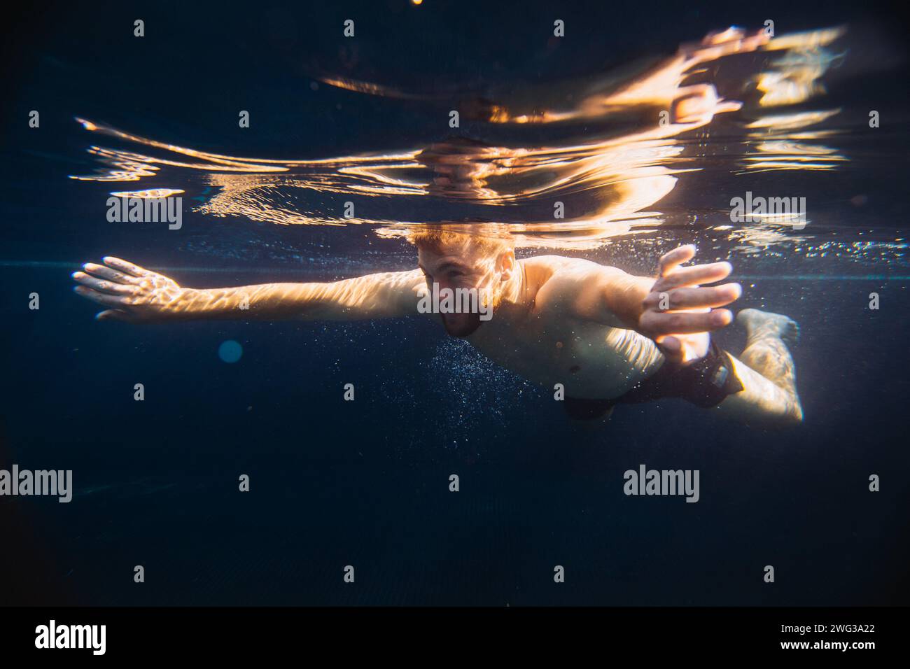 A handsome young man swims underwater in a swimming pool while on ...