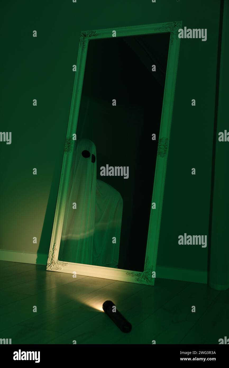 Creepy ghost. Woman covered with sheet in green light, reflection in ...