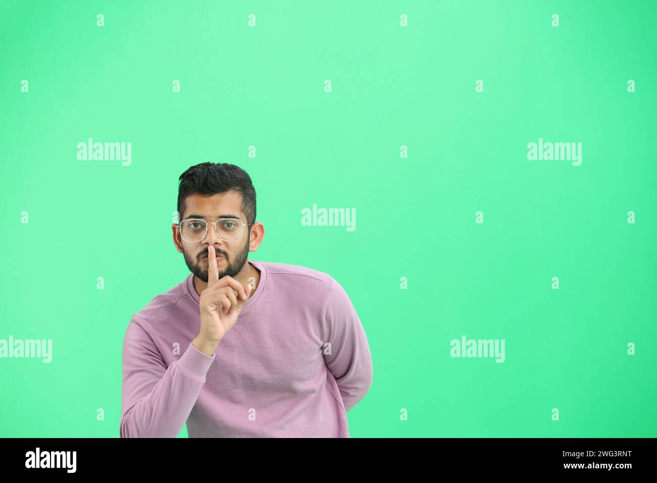 A man, on a green background, in close-up, shows a sign of silence ...