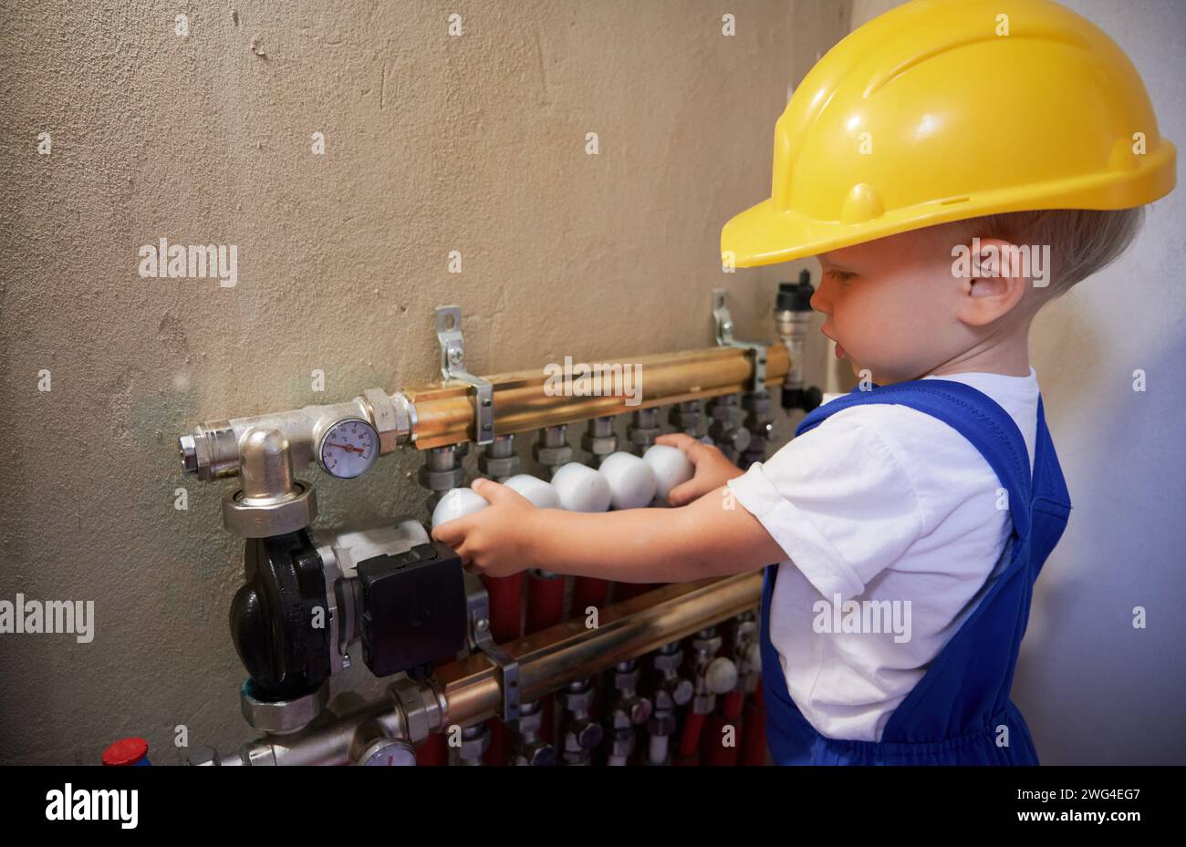 Baby boy in safety construction helmet checking plumbing installation ...