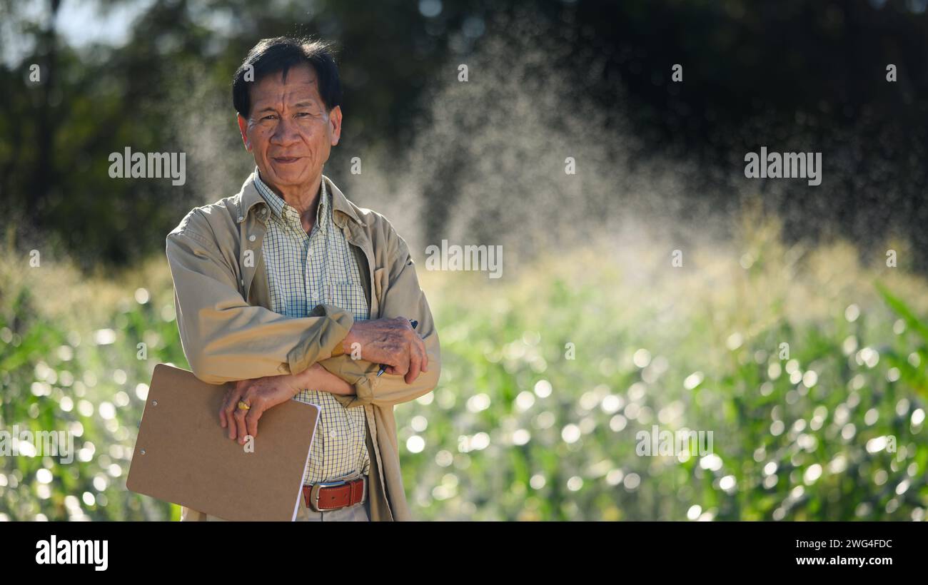 Successful senior farmer standing with crossed arms in front of field ...