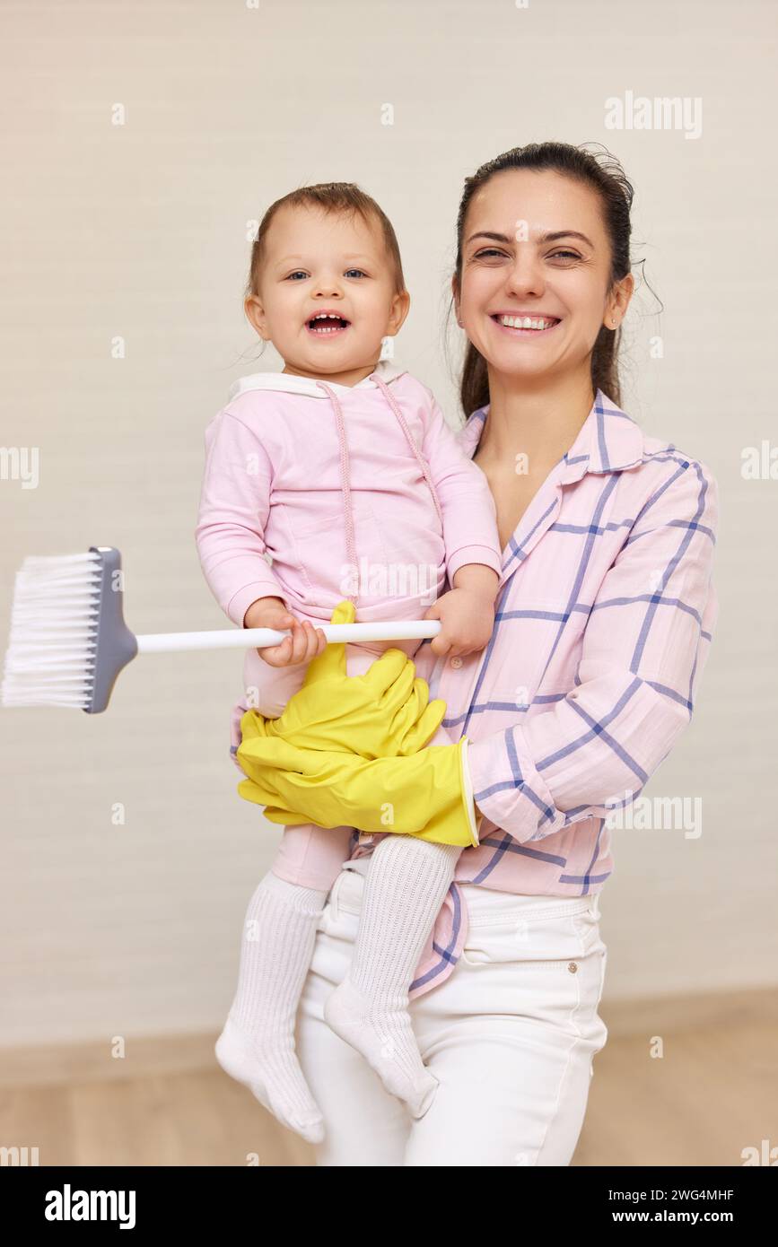 happy mother housewife is holding cute baby girl and doing housework at ...