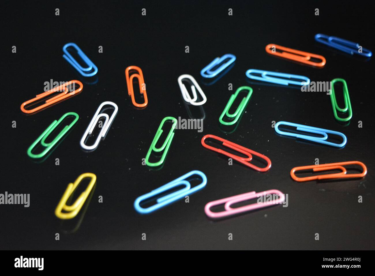 Many bright glossy colorful paper clips lie on a black glossy surface ...