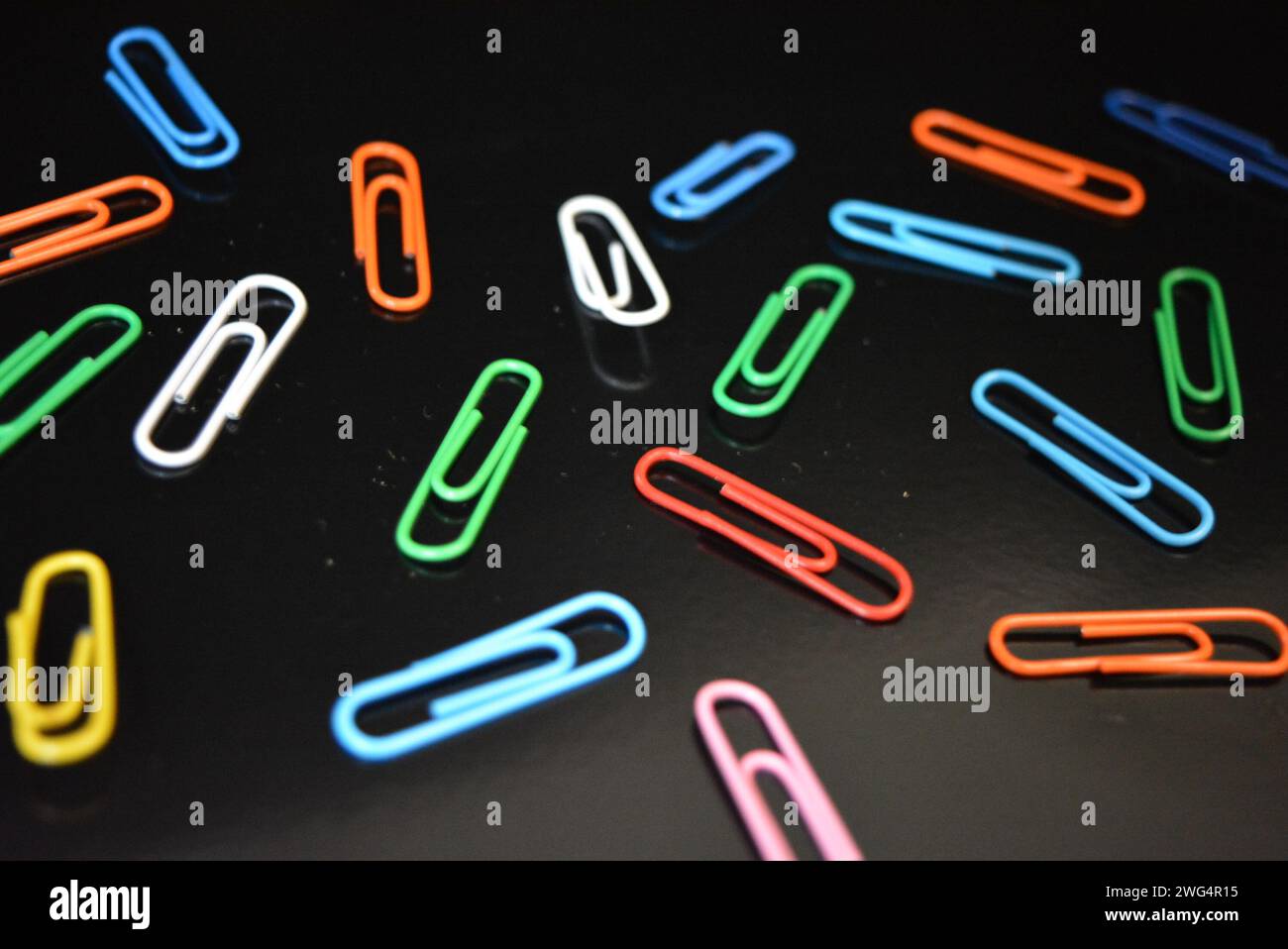 Many bright glossy colorful paper clips lie on a black glossy surface ...