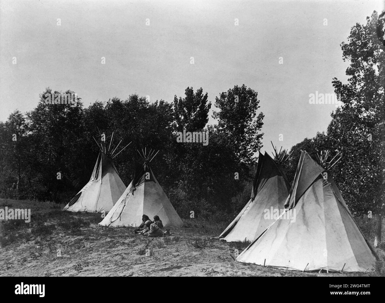 An Assiniboin camp containing four tepees with Indians seated on ground ...