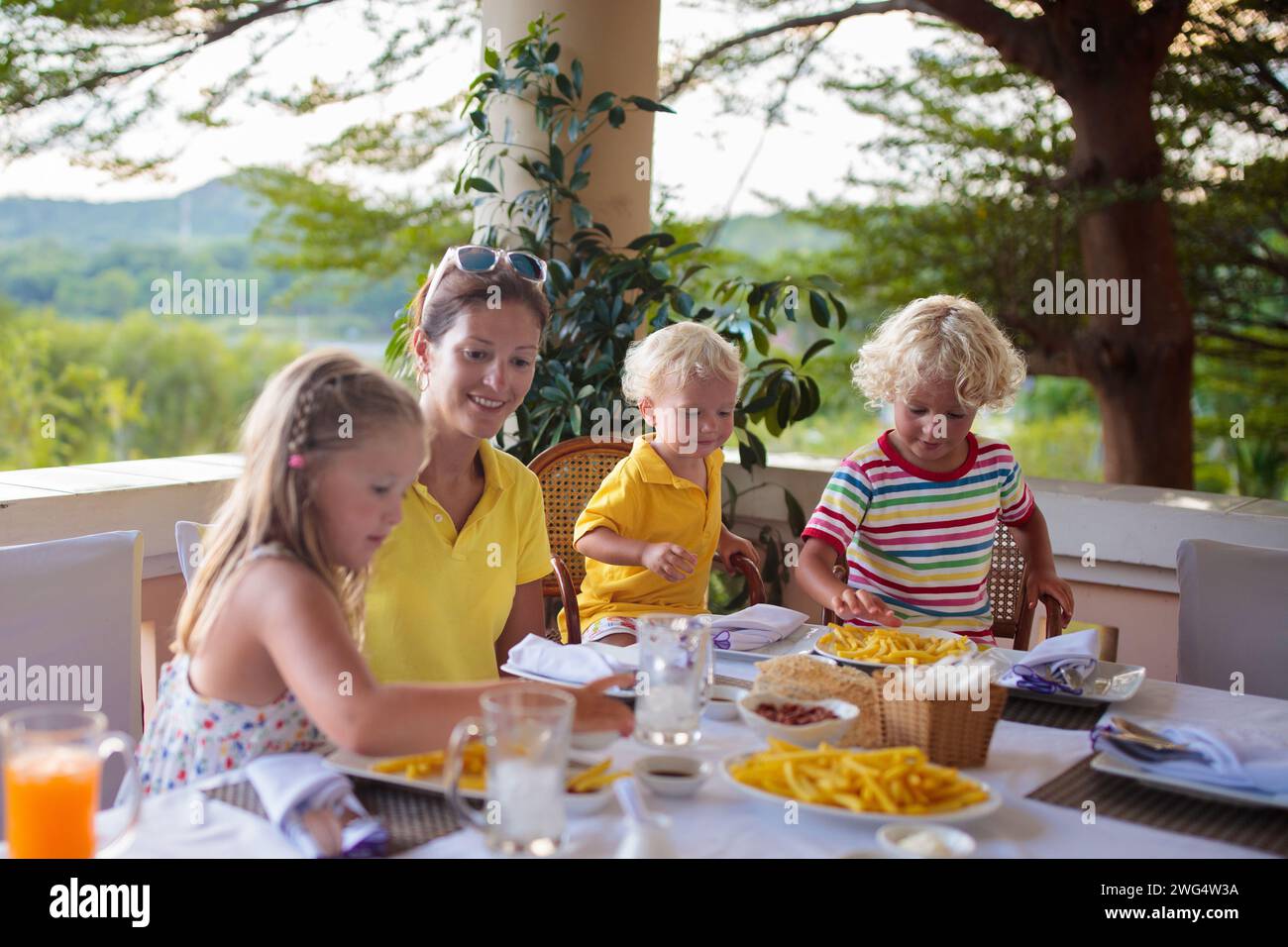 Family having dinner on outdoor patio. Mother and kids eating breakfast ...