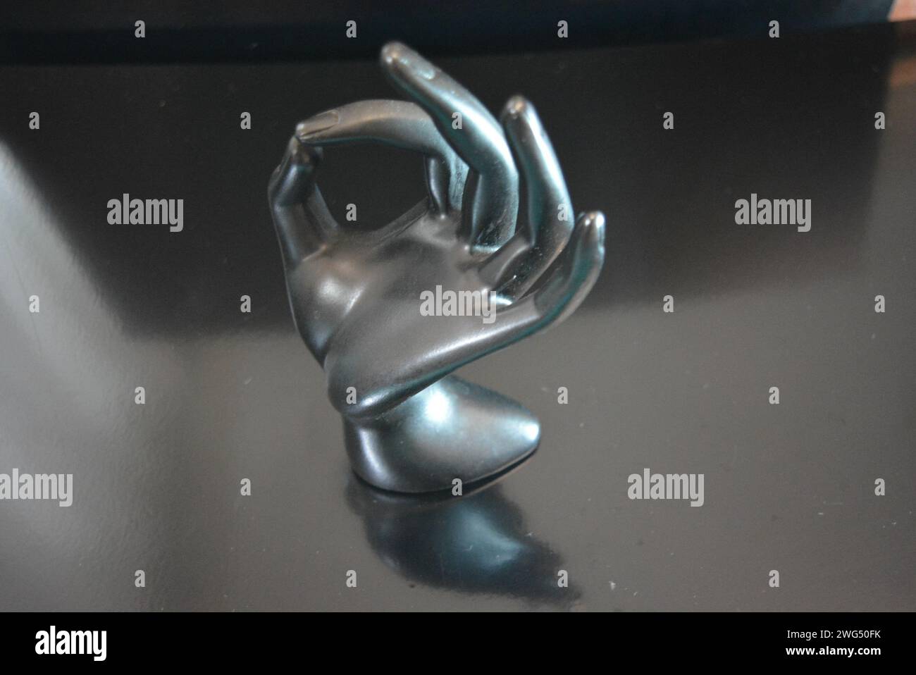 A matte black ceramic hand-shaped statuette is located on a matte black ...
