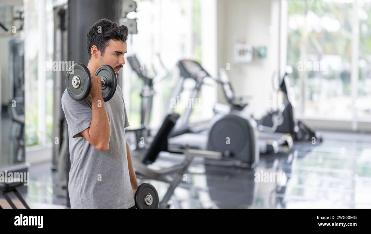 Focused young man performing a bicep curl in a modern gym, showcasing ...