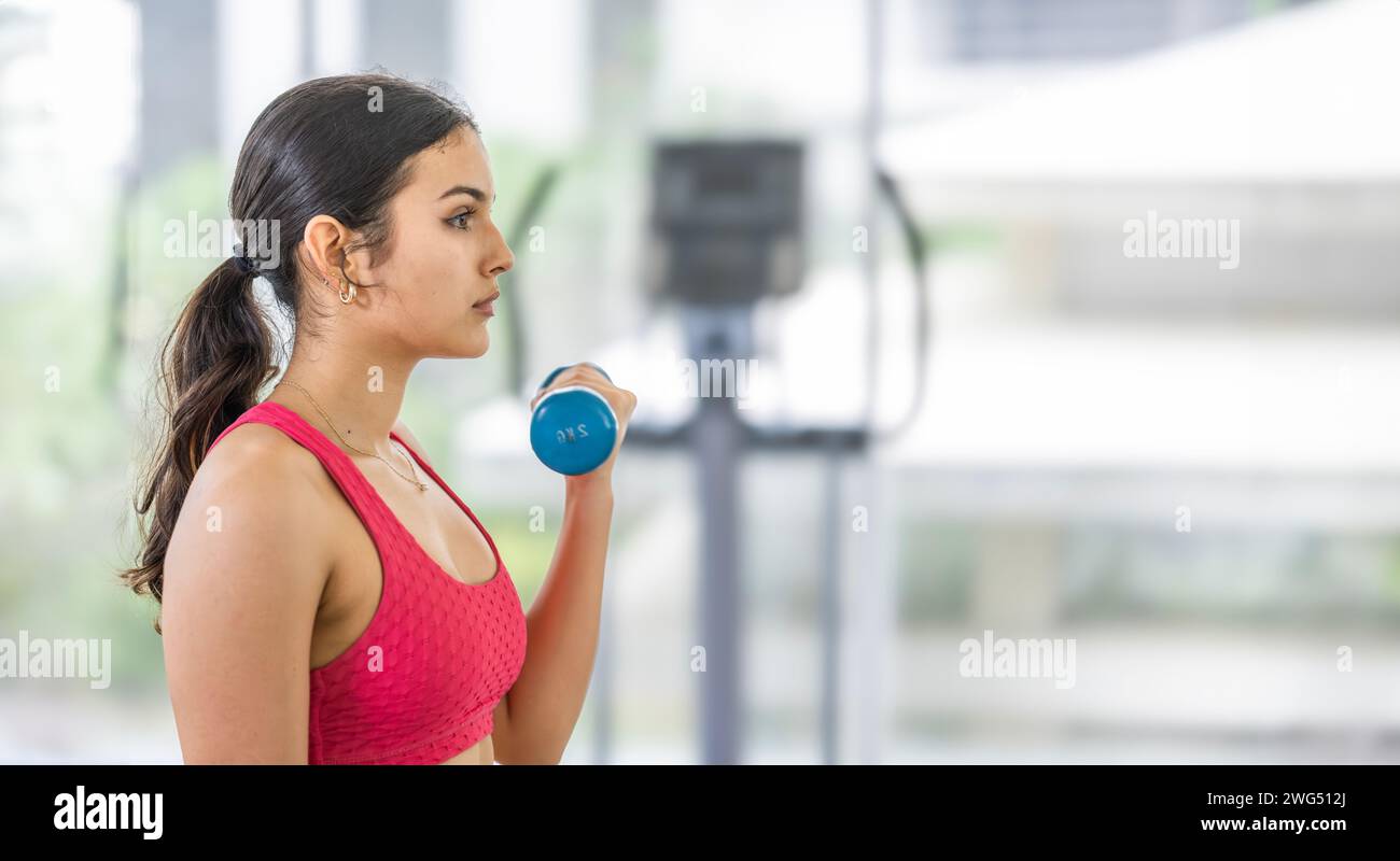Young Focused female athlete performing a bicep curl with a blue ...