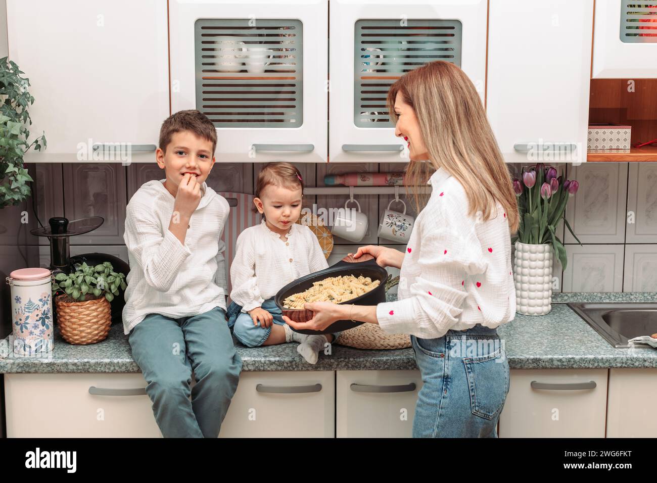 Mom and her children in the kitchen with pasta in the pan for dinner ...
