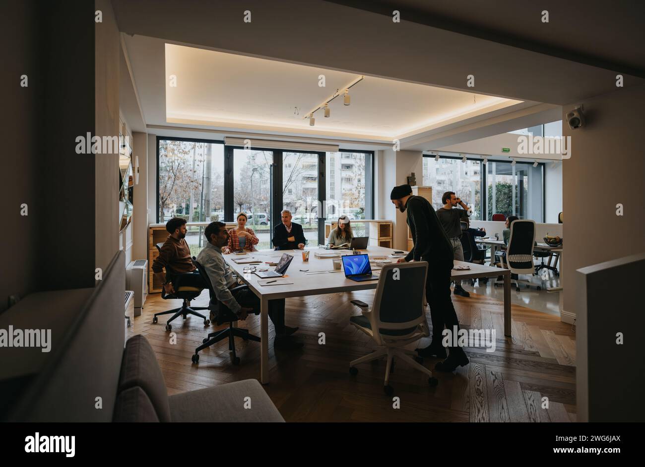 Collaborative team in a well-lit office engaging in a business meeting with laptops, discussions ...