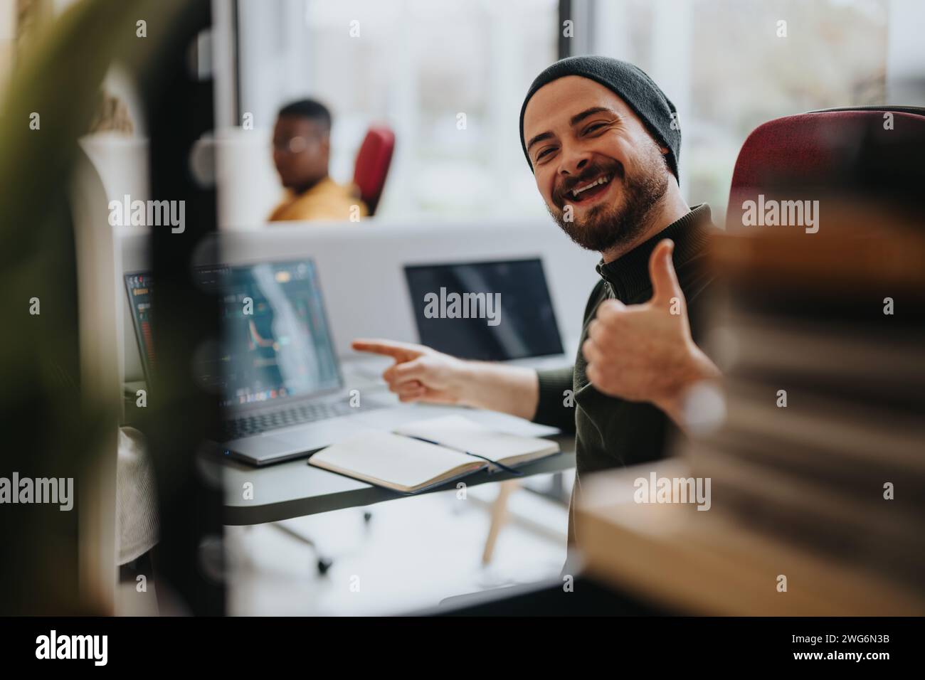 Cheerful bearded man giving thumbs up in modern office workspace while ...