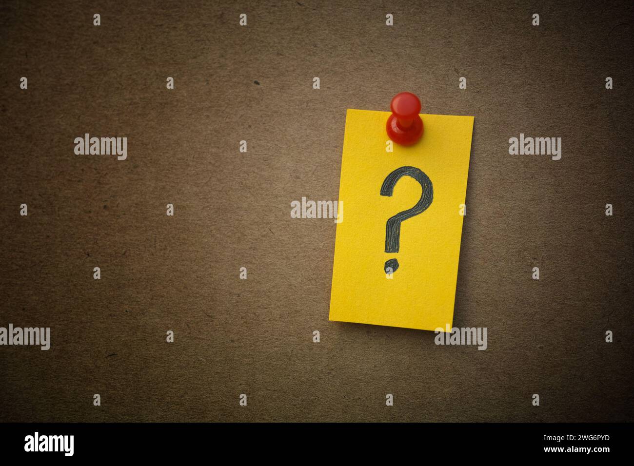 A yellow paper note with a question mark on it pinned to a cardboard ...