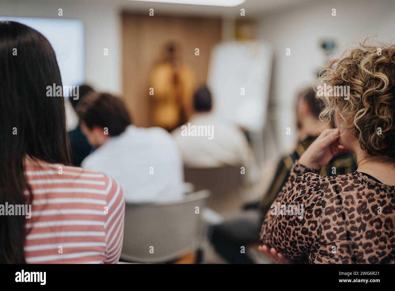 A diverse group of attendees carefully listening to an out-of-focus ...