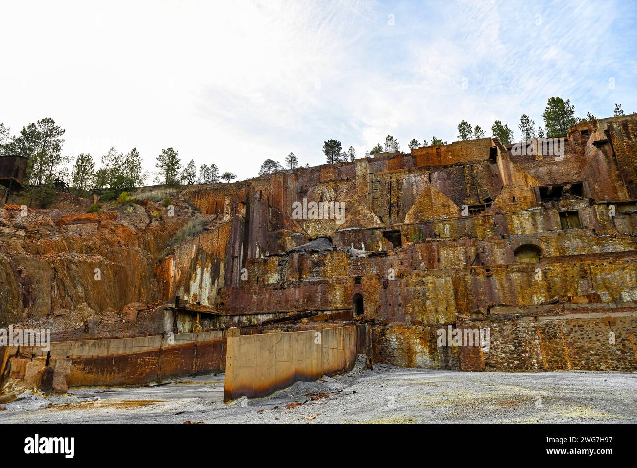 Decaying remains of mining structures stand over a stagnant water body ...