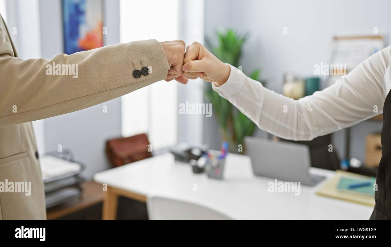 Two coworkers performing a fist bump in an office setting, signifying ...