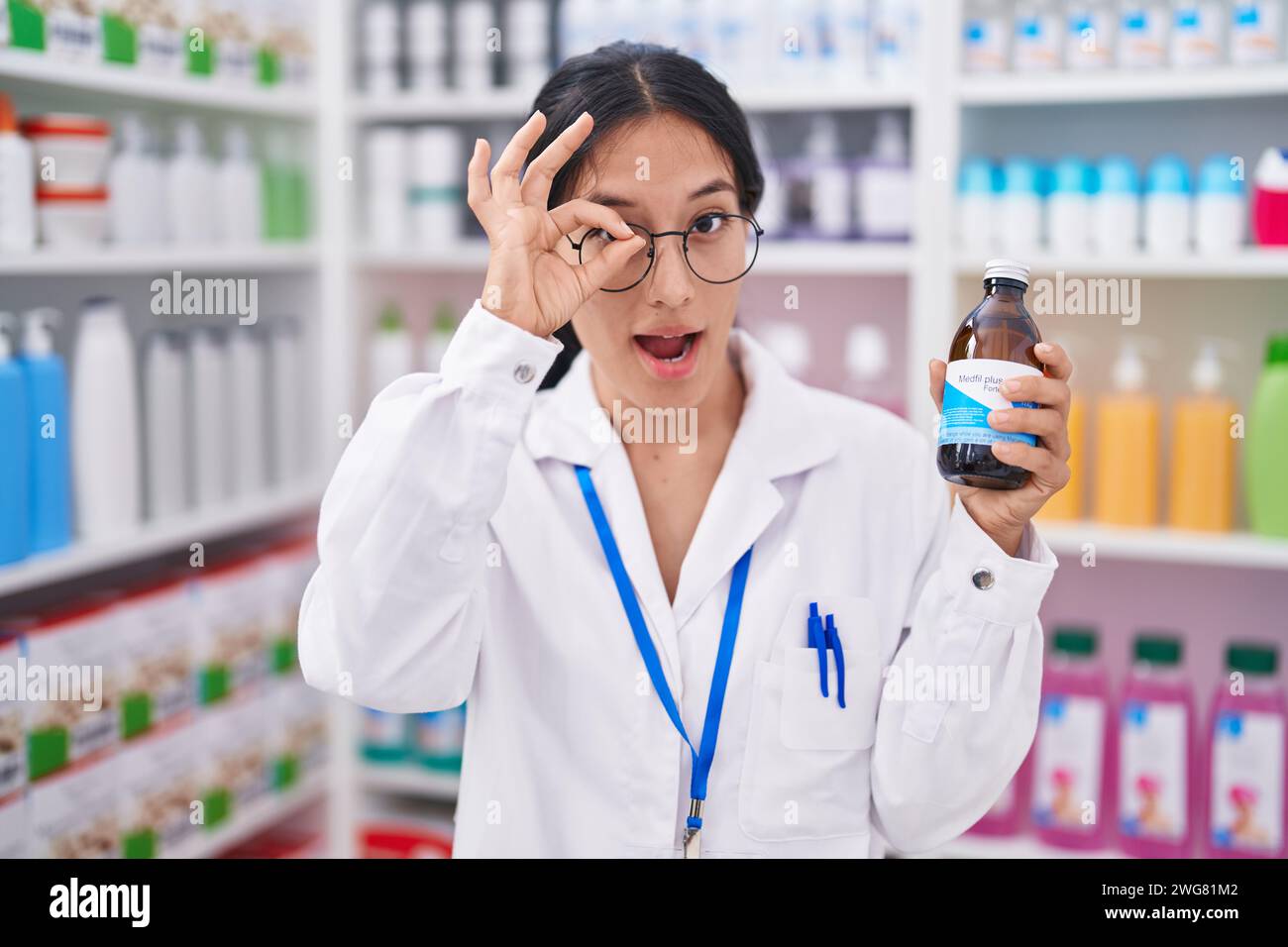 Young hispanic woman working at pharmacy drugstore holding syrup ...