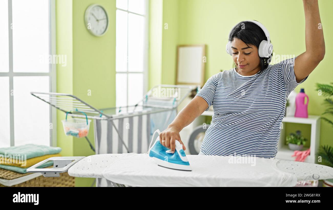 Hispanic woman joyfully ironing clothes in a bright laundry room ...
