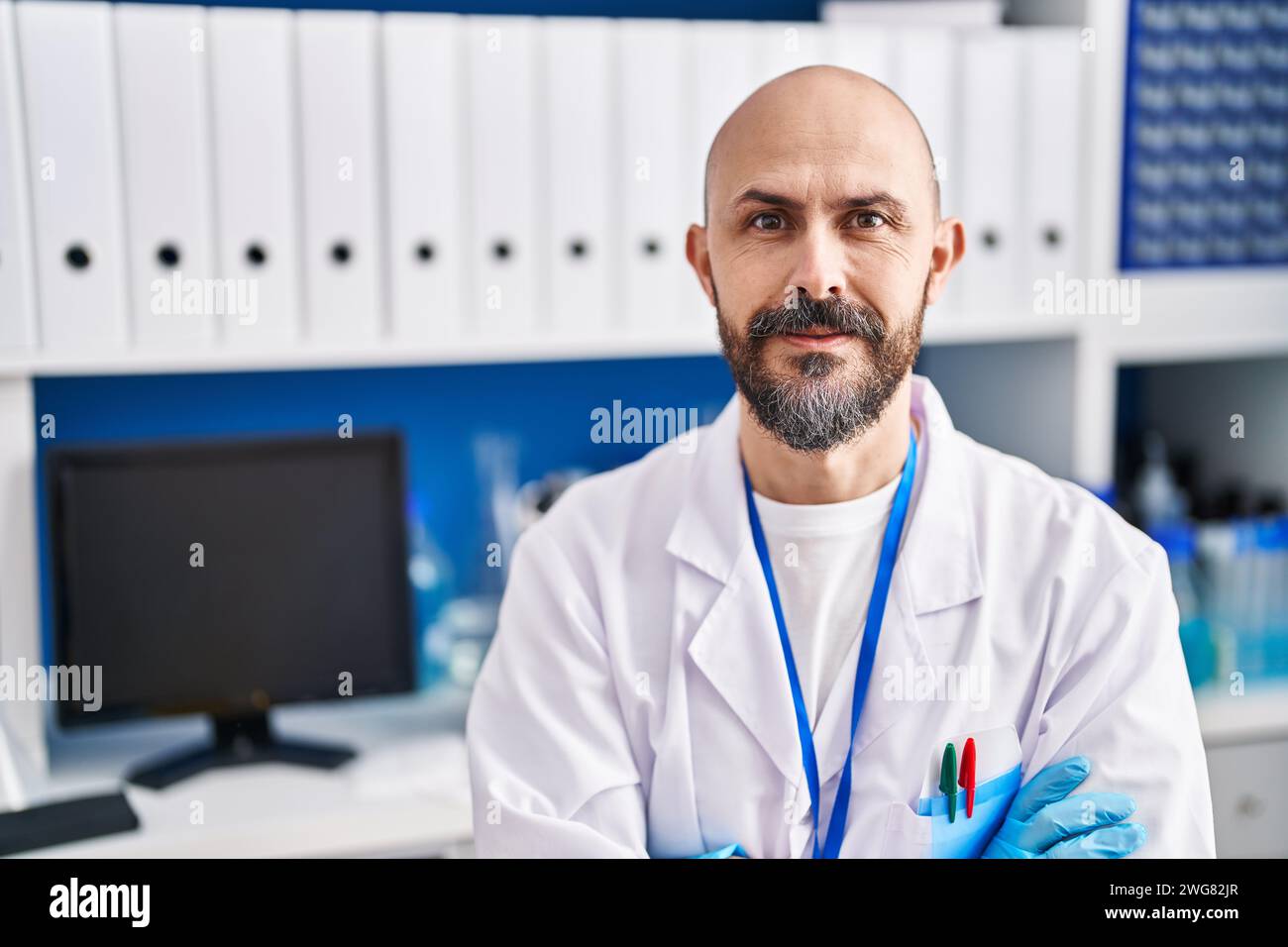Young bald man scientist smiling confident sitting with arms crossed gesture at laboratory Stock ...