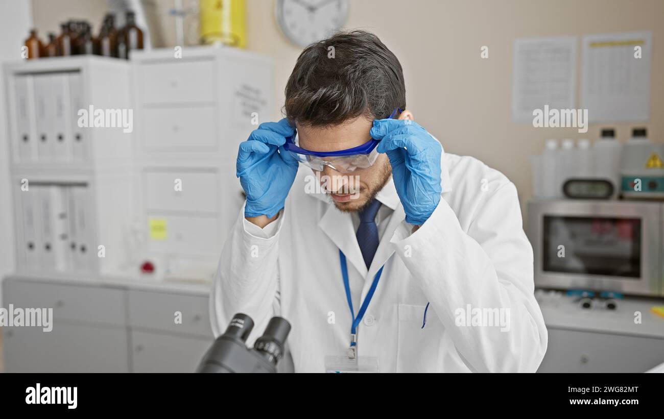 Hispanic man in lab coat adjusting safety goggles indoors at a ...