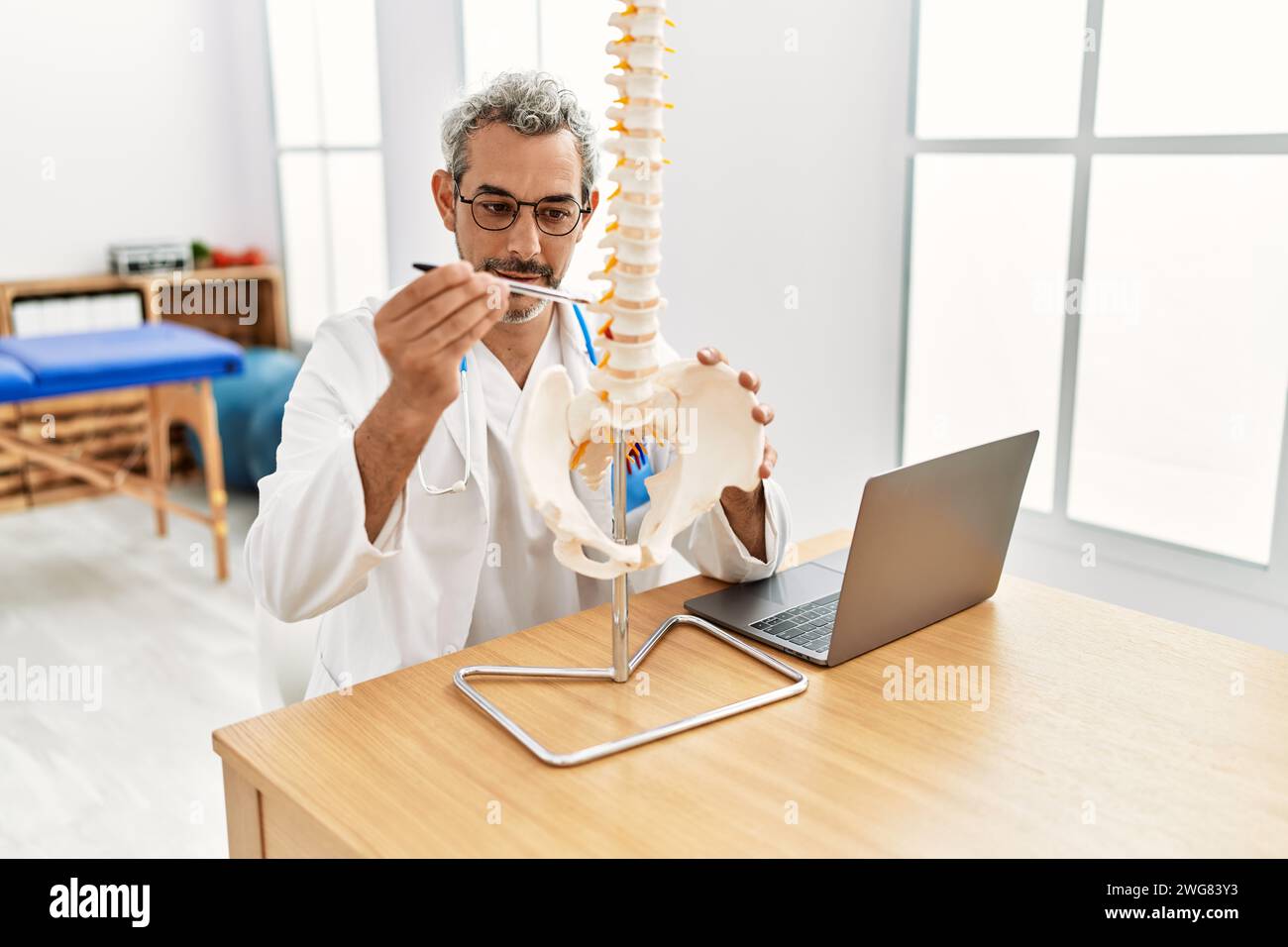 Middle age grey-haired man doctor holding anatomical model of spinal ...