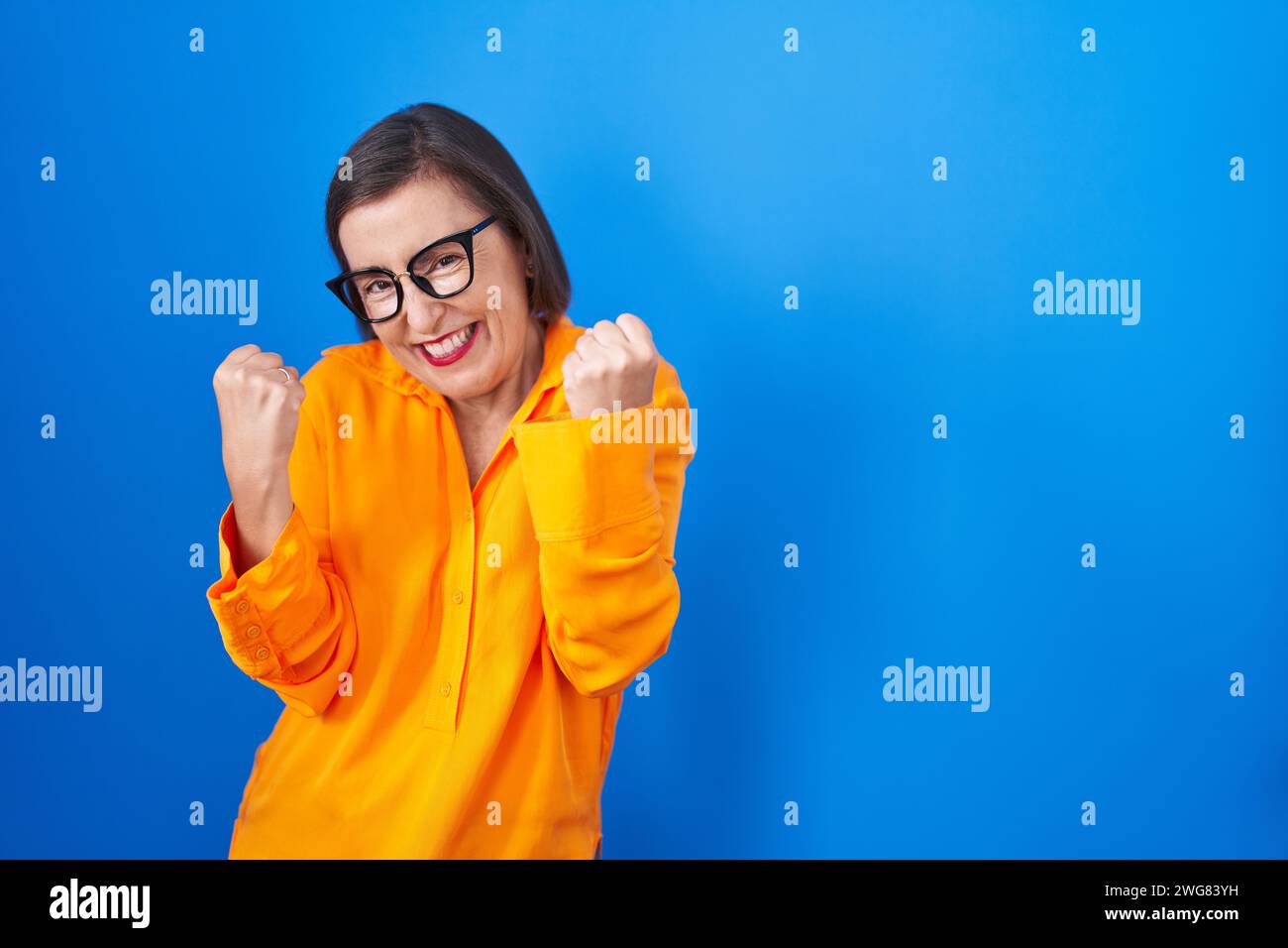 Middle age hispanic woman wearing glasses standing over blue background ...