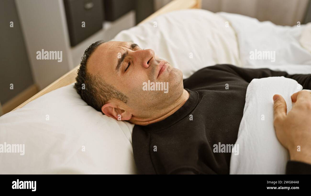 Hispanic man resting indoors on a bed with eyes closed in a modern ...