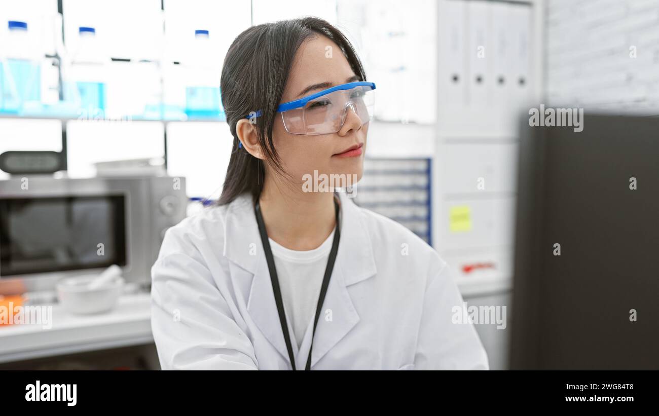 A young asian woman scientist wearing safety goggles works in a ...