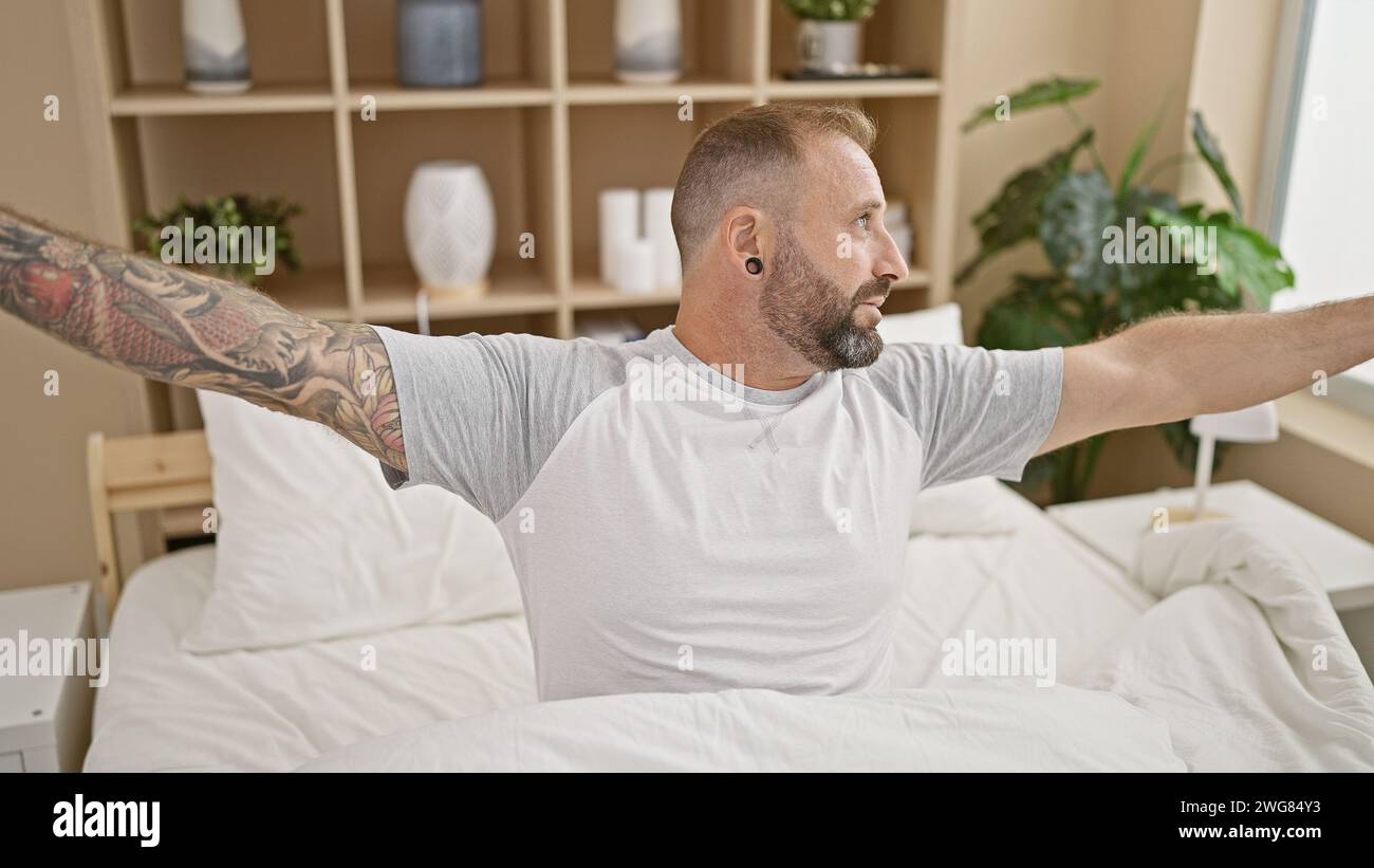 Handsome young man stretching arms in cozy comfort of bed, waking up in the morning, enjoying ...