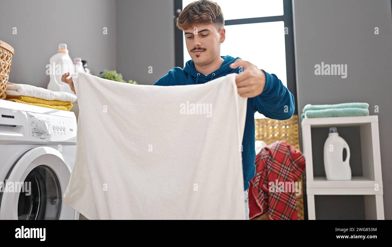 Young hispanic man washing clothes folding towel at laundry room Stock ...