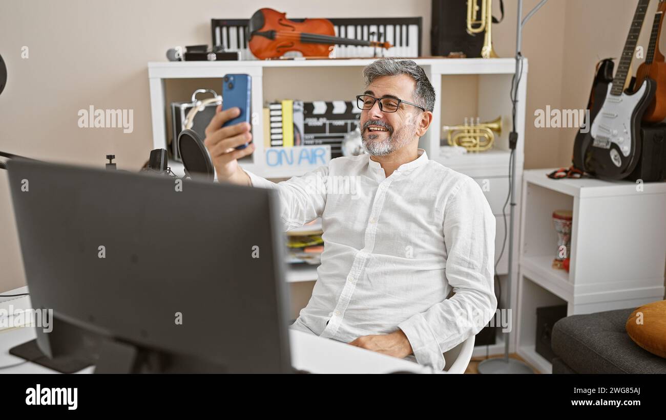 Handsome, young hispanic man, grey-haired radio news reporter making a smiling selfie with his ...