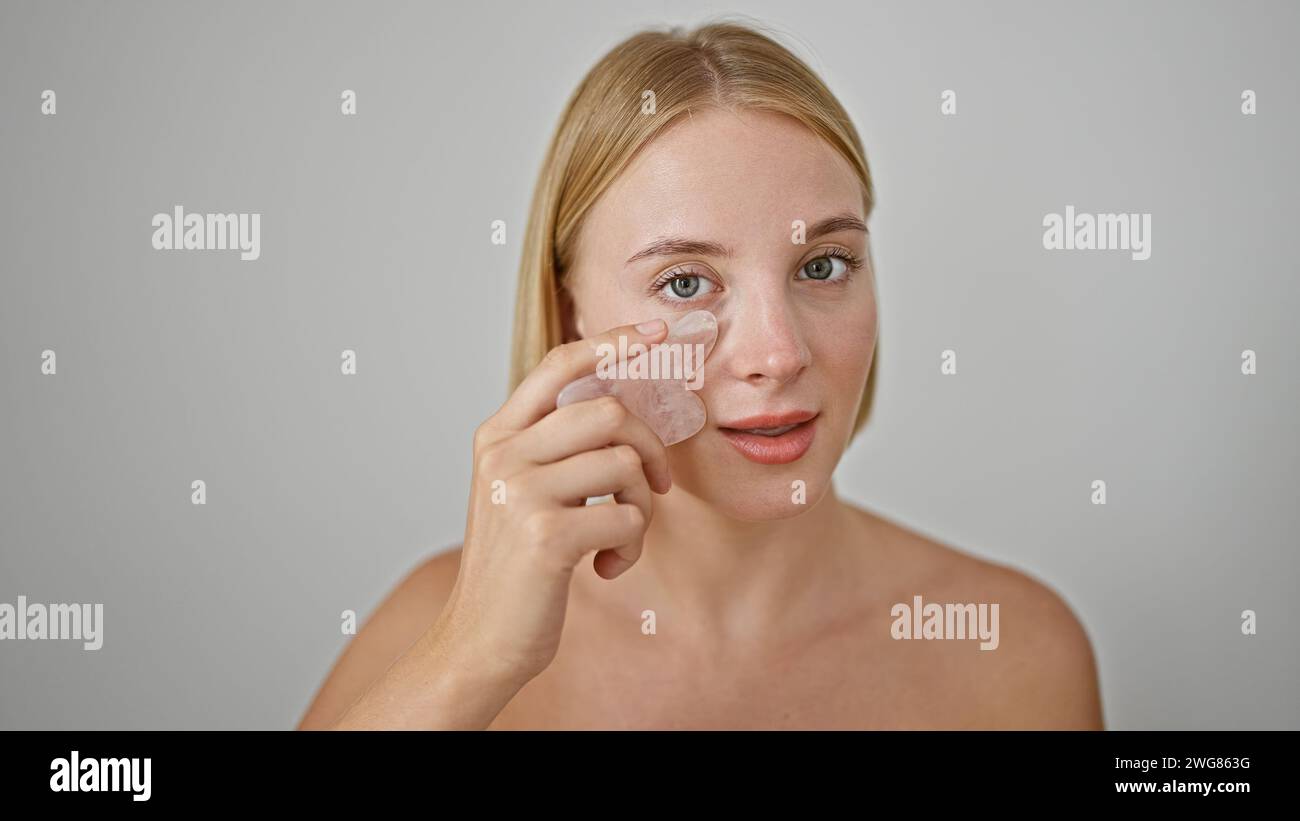 Young blonde woman massaging face using pink quartz gua sha over ...