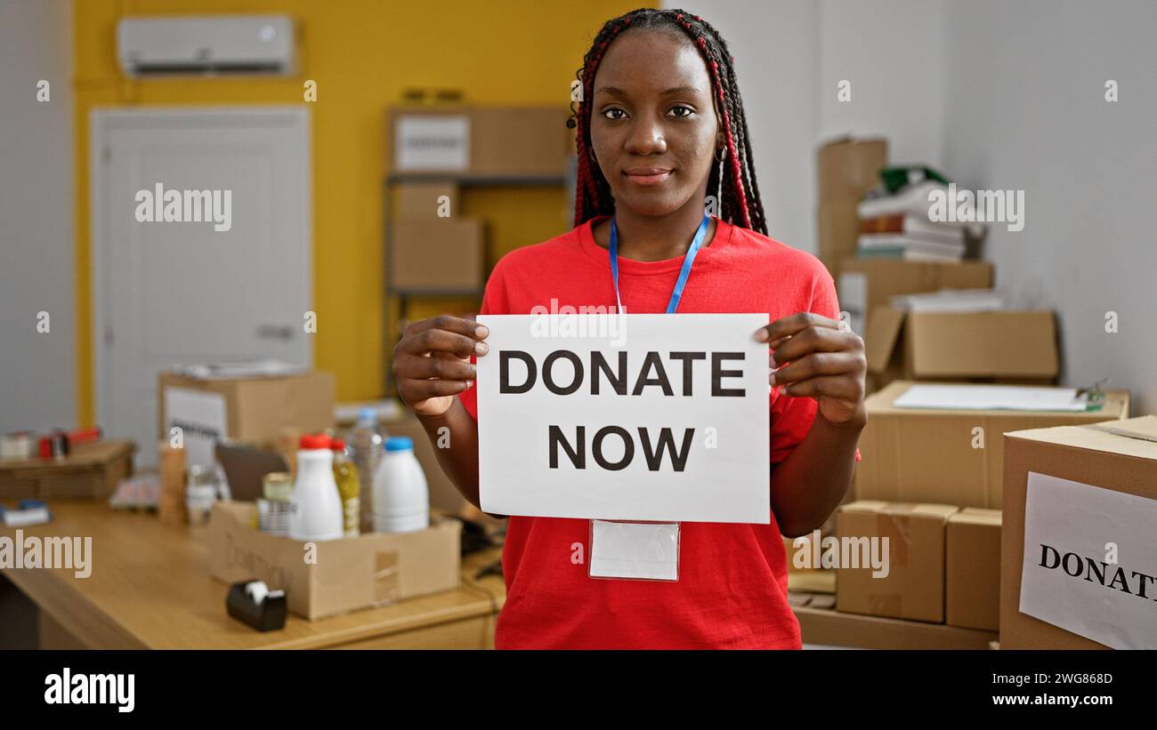 Serious-faced african american woman volunteer holding 'donate now' sign at charity center ...