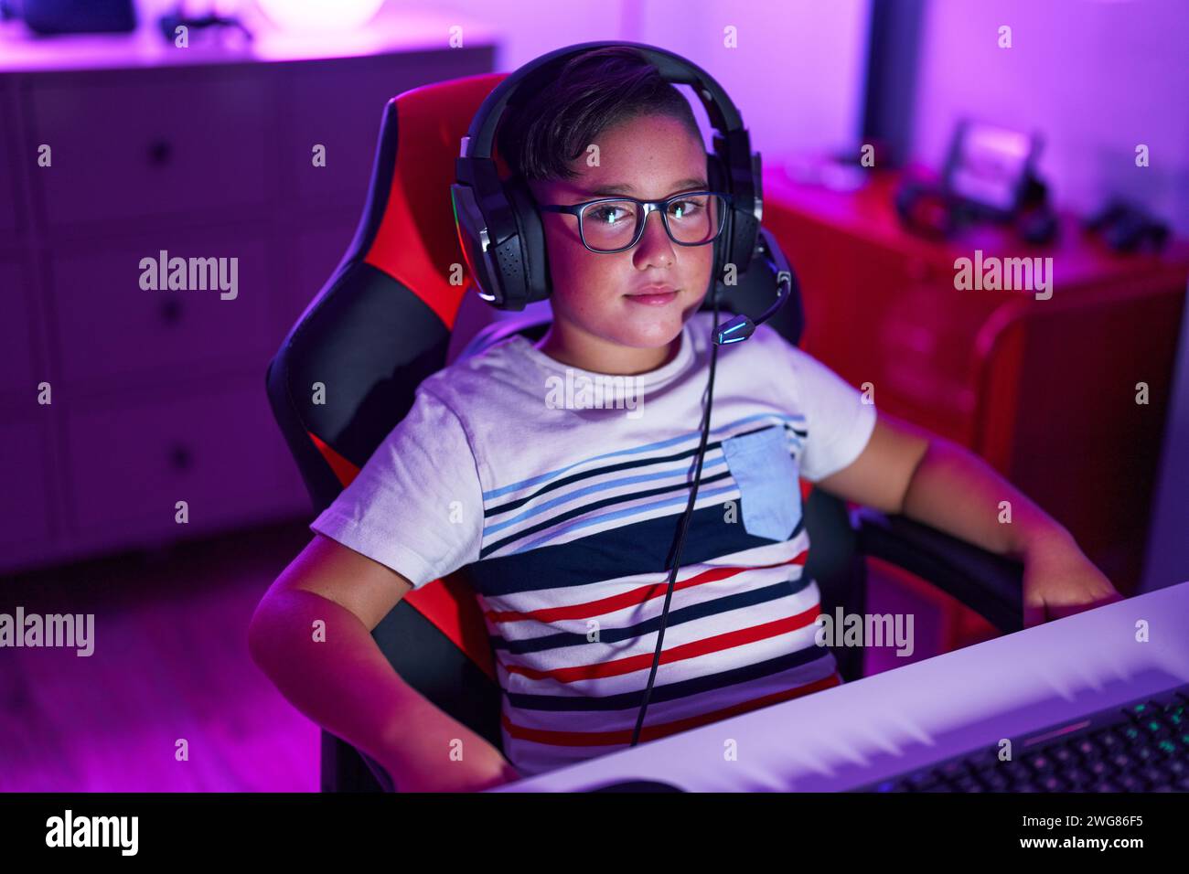 Adorable hispanic boy streamer sitting on table with serious expression ...