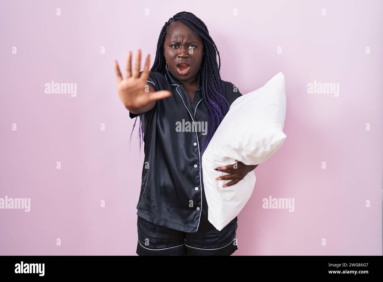 Young african woman wearing pijama hugging pillow doing stop gesture ...