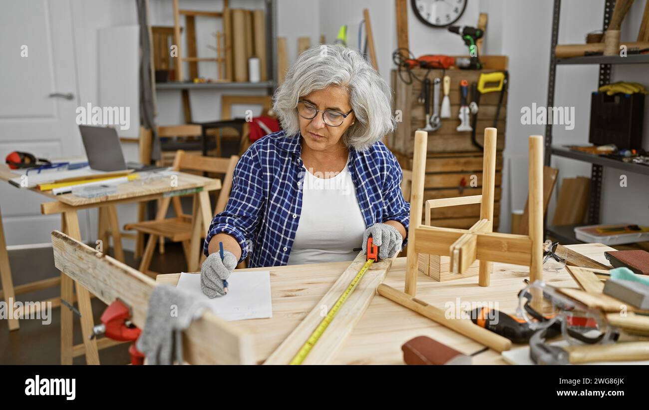 Mature woman measuring wood with tape in a cluttered carpentry workshop ...