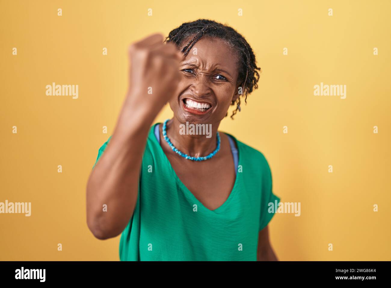 African woman with dreadlocks standing over yellow background angry and ...