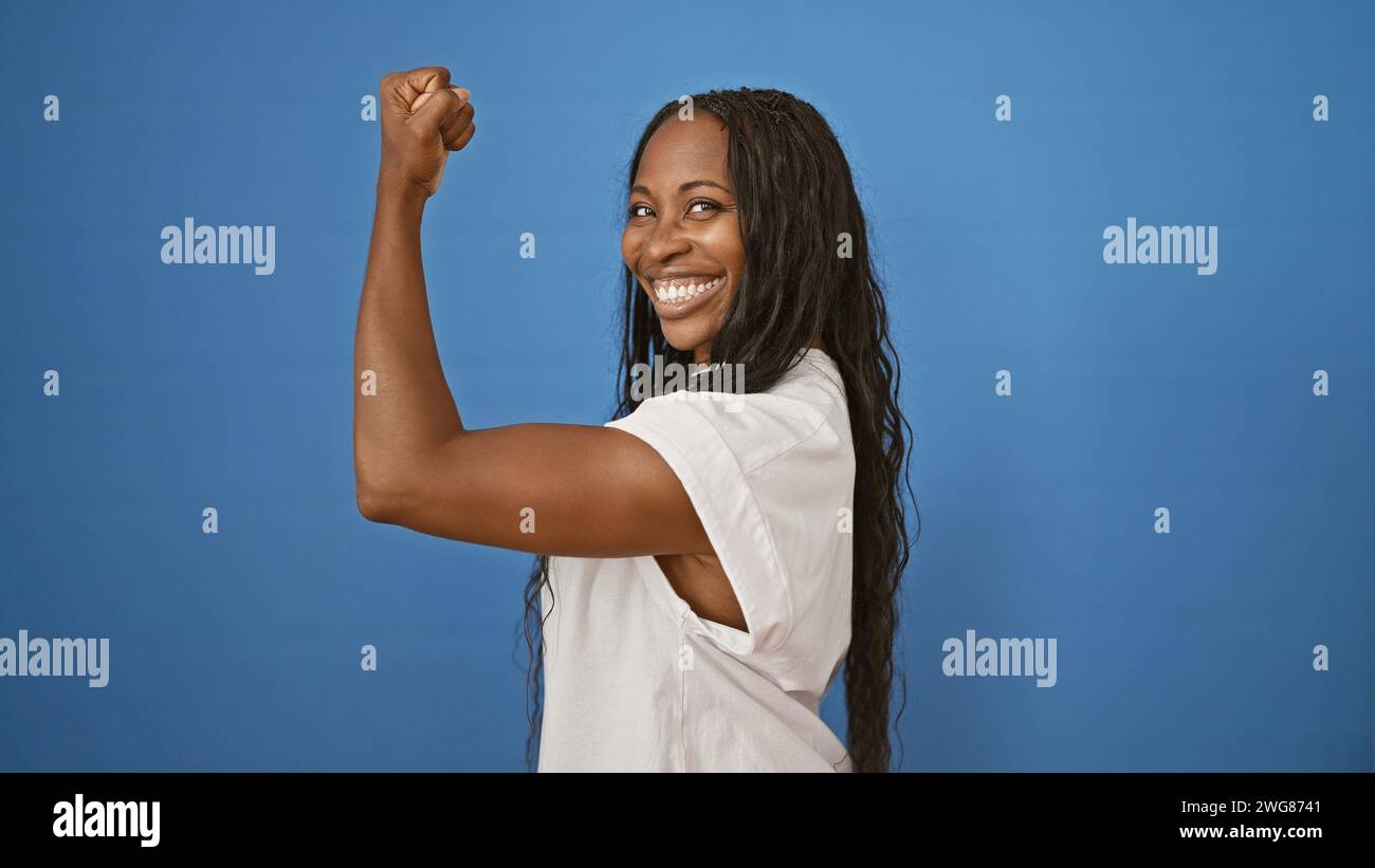 Happy african woman flexing her muscle confidently against a blue ...