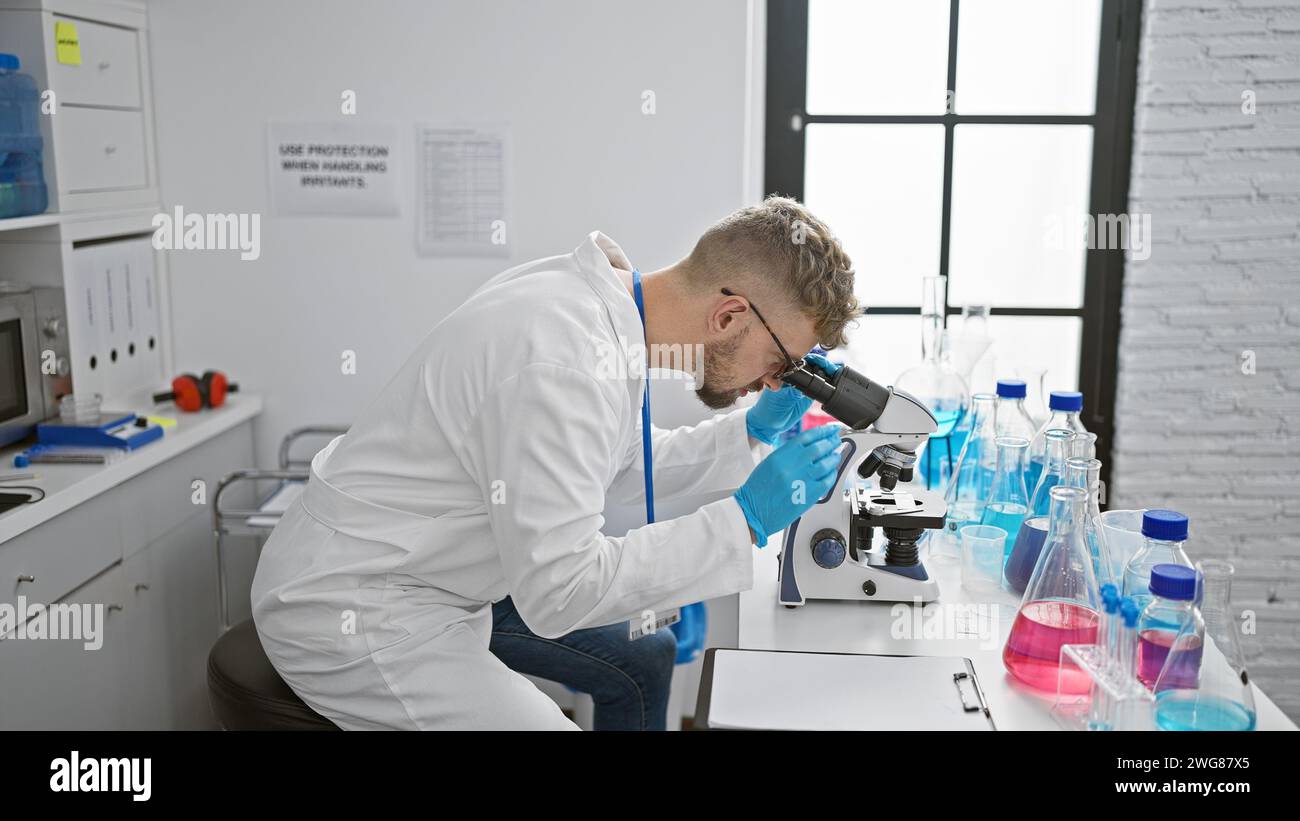 A young caucasian man with a beard examines samples through a ...