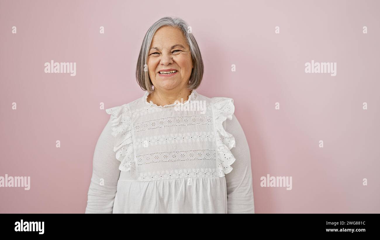 A cheerful middle-aged woman with grey hair stands against a pink ...