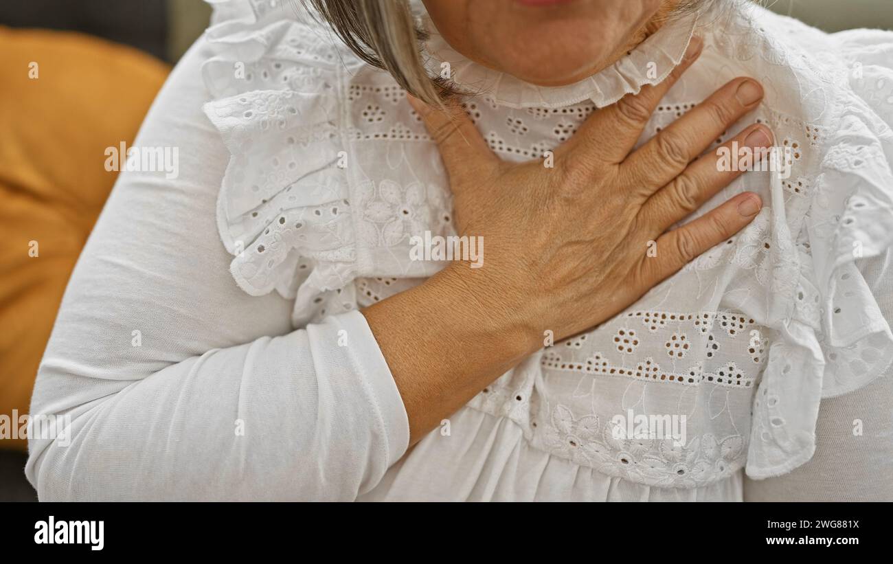 Mature woman experiencing chest pain while sitting in a living room ...