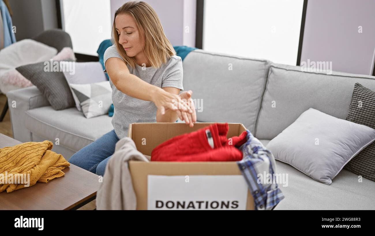 Attractive, young blonde woman sitting comfortably on her living room ...