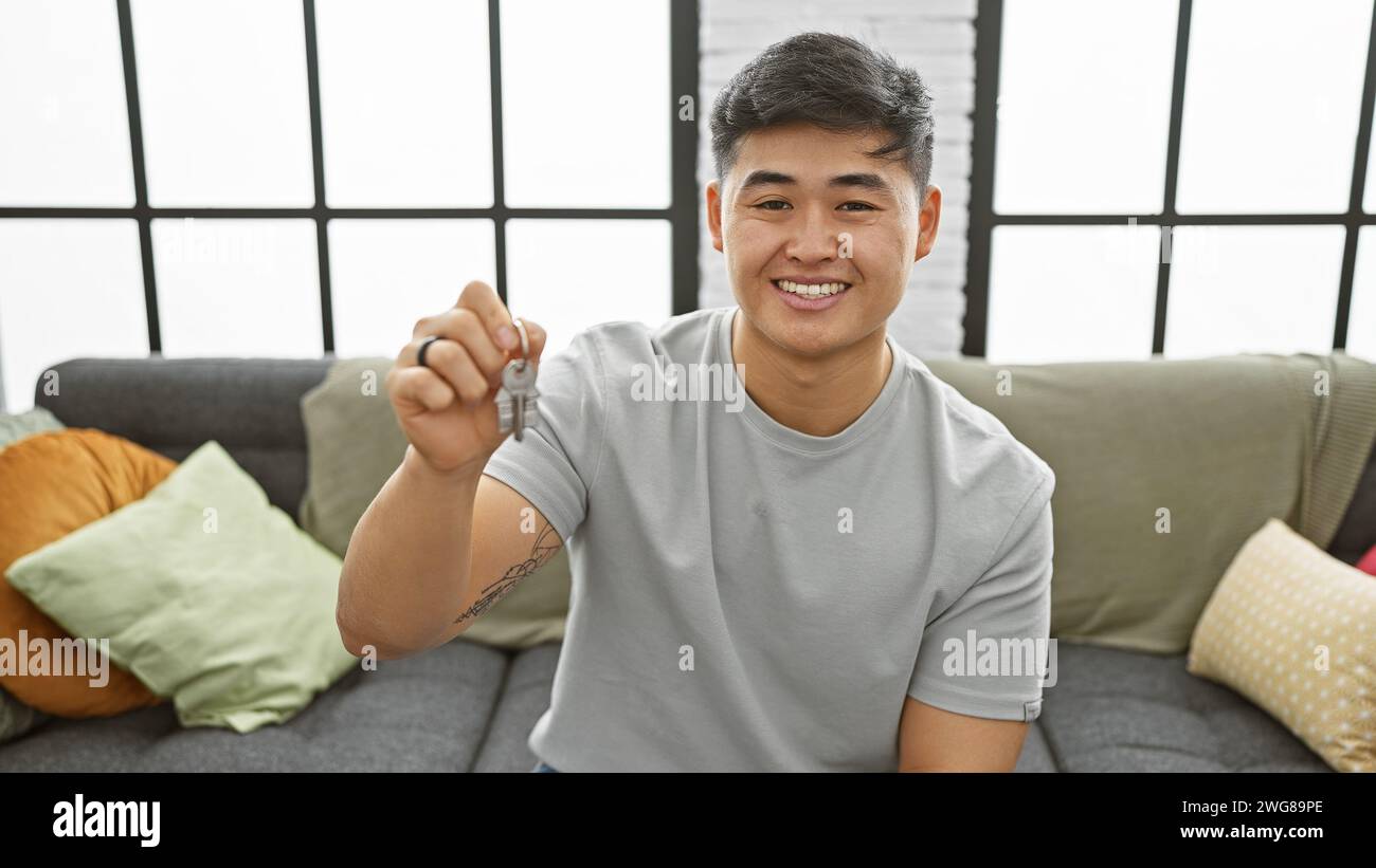 Smiling asian man holding key in modern living room showcasing ...