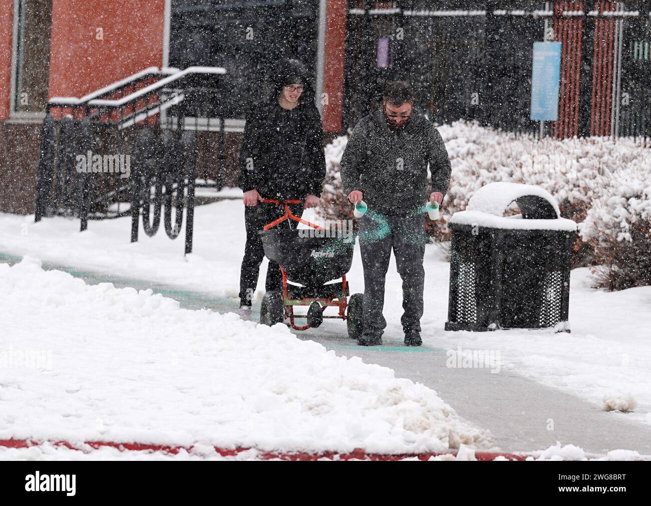 Workers spread deicer on a path cleared for members to a gym as a ...