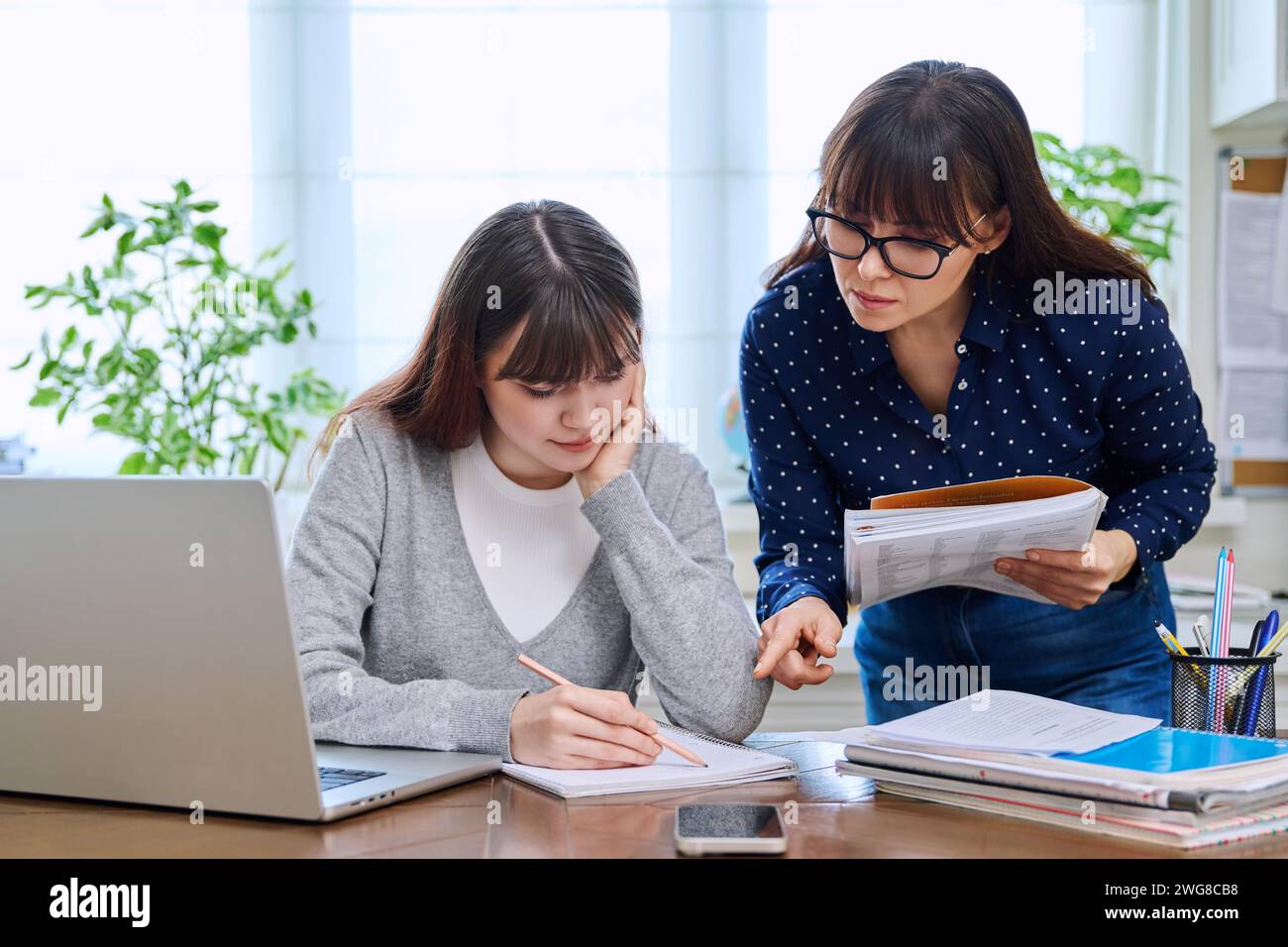 Teenage student studying at desk with computer, trainer mentor helping ...