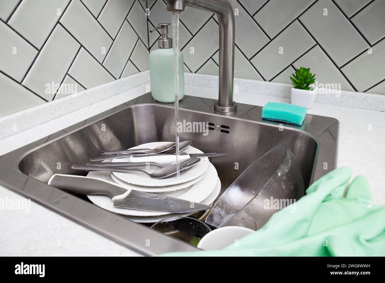 A stainless steel sink contains a stack of used plates and utensils ...