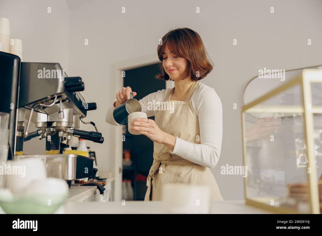 Pretty female barista makes coffee and pours it into a mug while ...