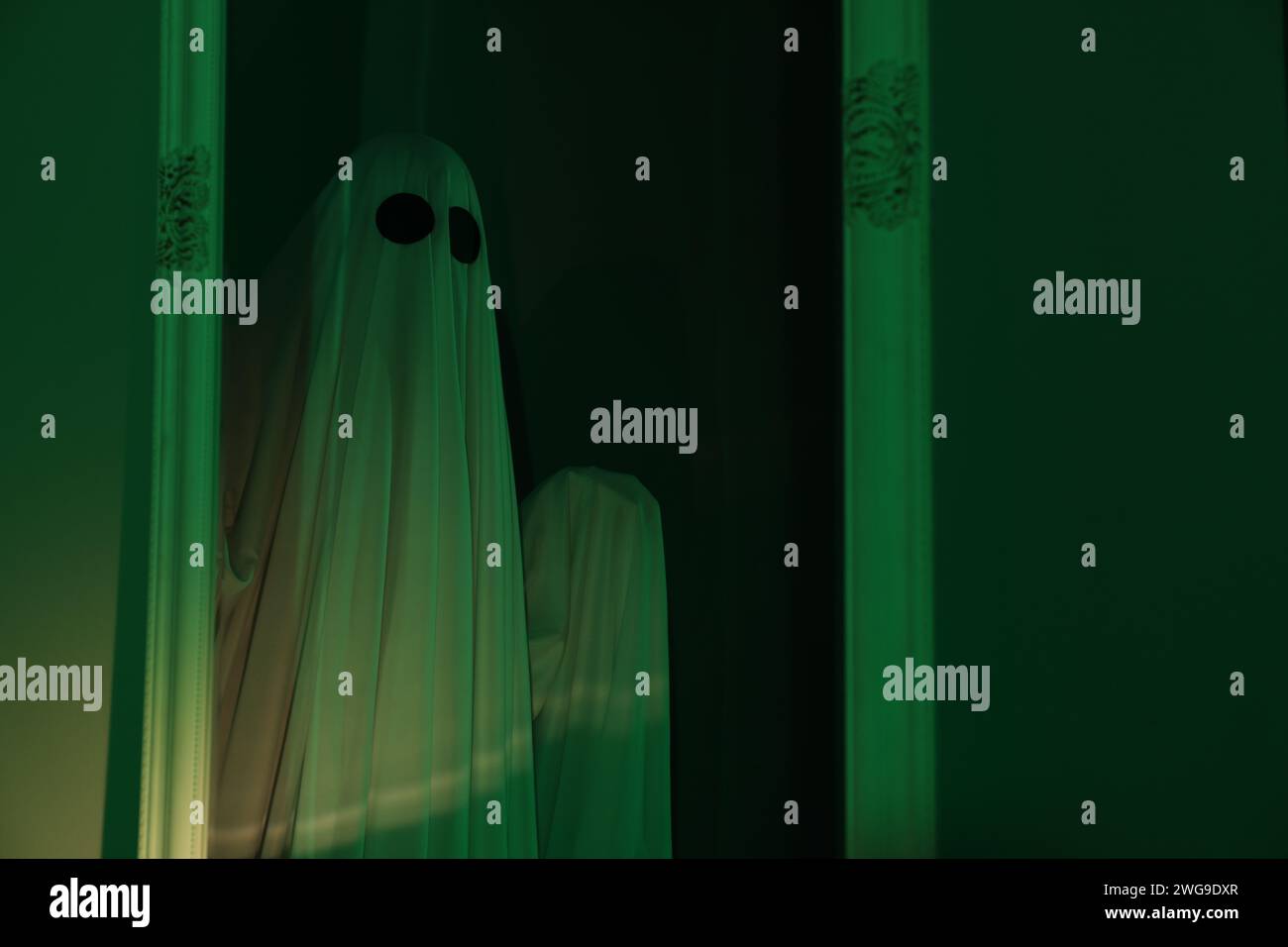 Creepy ghost. Woman covered with sheet in green light, reflection in ...