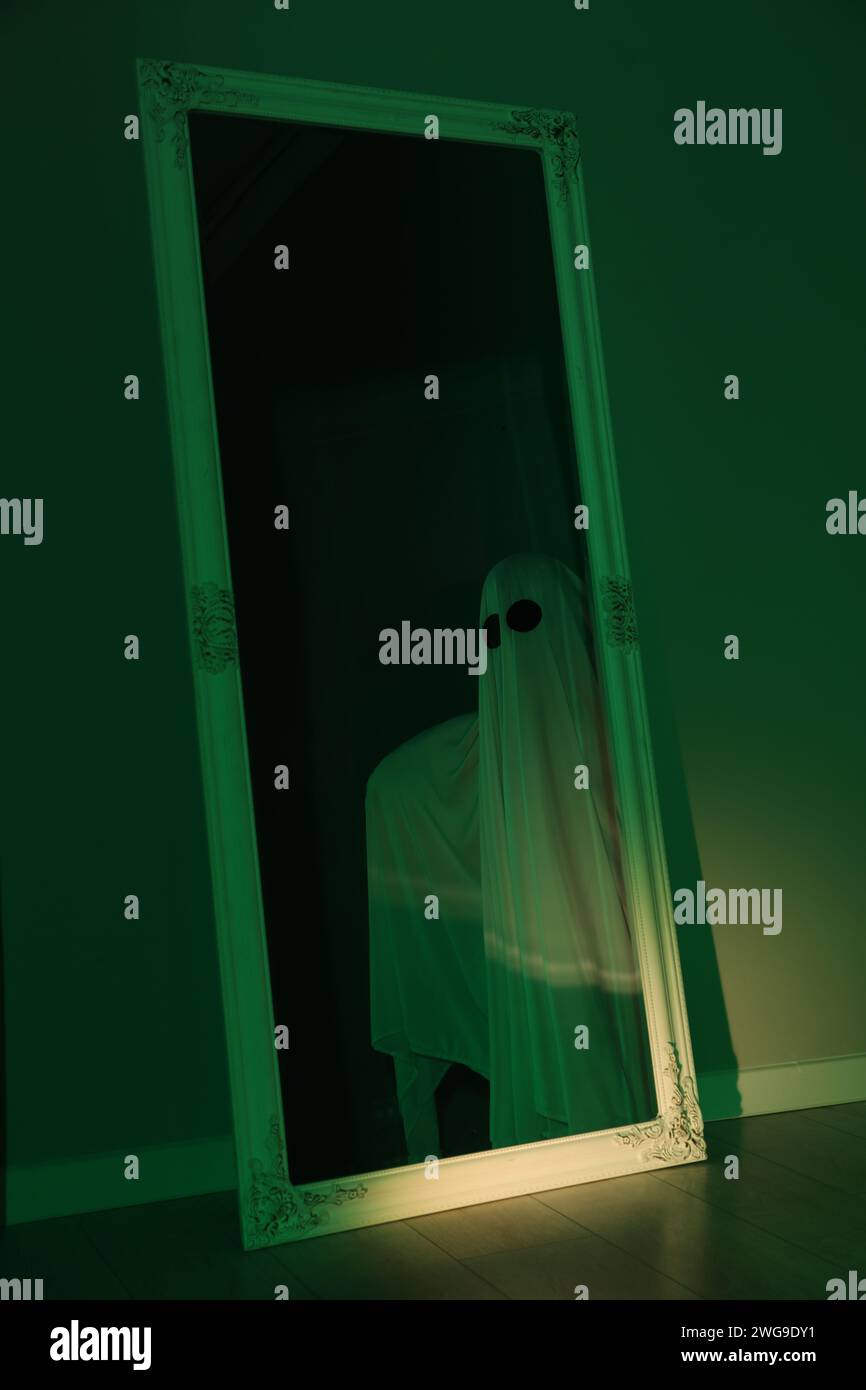 Creepy ghost. Woman covered with sheet in green light, reflection in ...